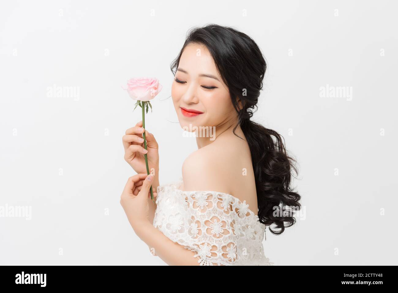 Profile portrait of a beautiful young woman smelling pink rose ...