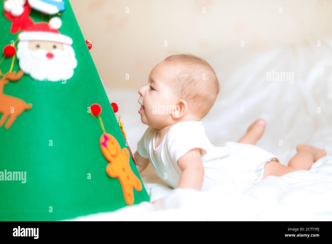 Little baby infant. Playing with a Christmas tree. lying on the bed ...