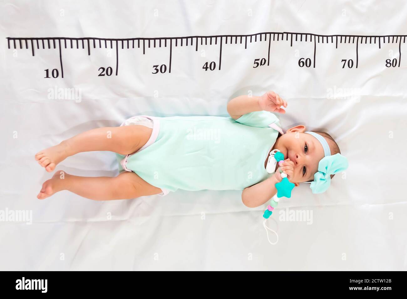 A three month baby in mint green clothes lying on a bed on which a ...