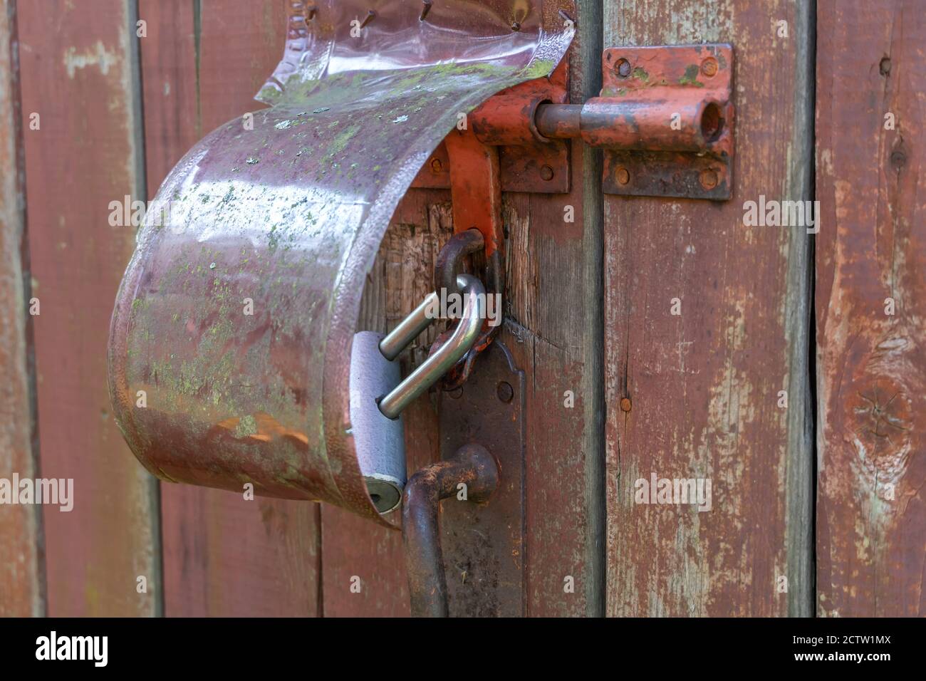 metal lock with rain protection hanging from an old wooden door close ...