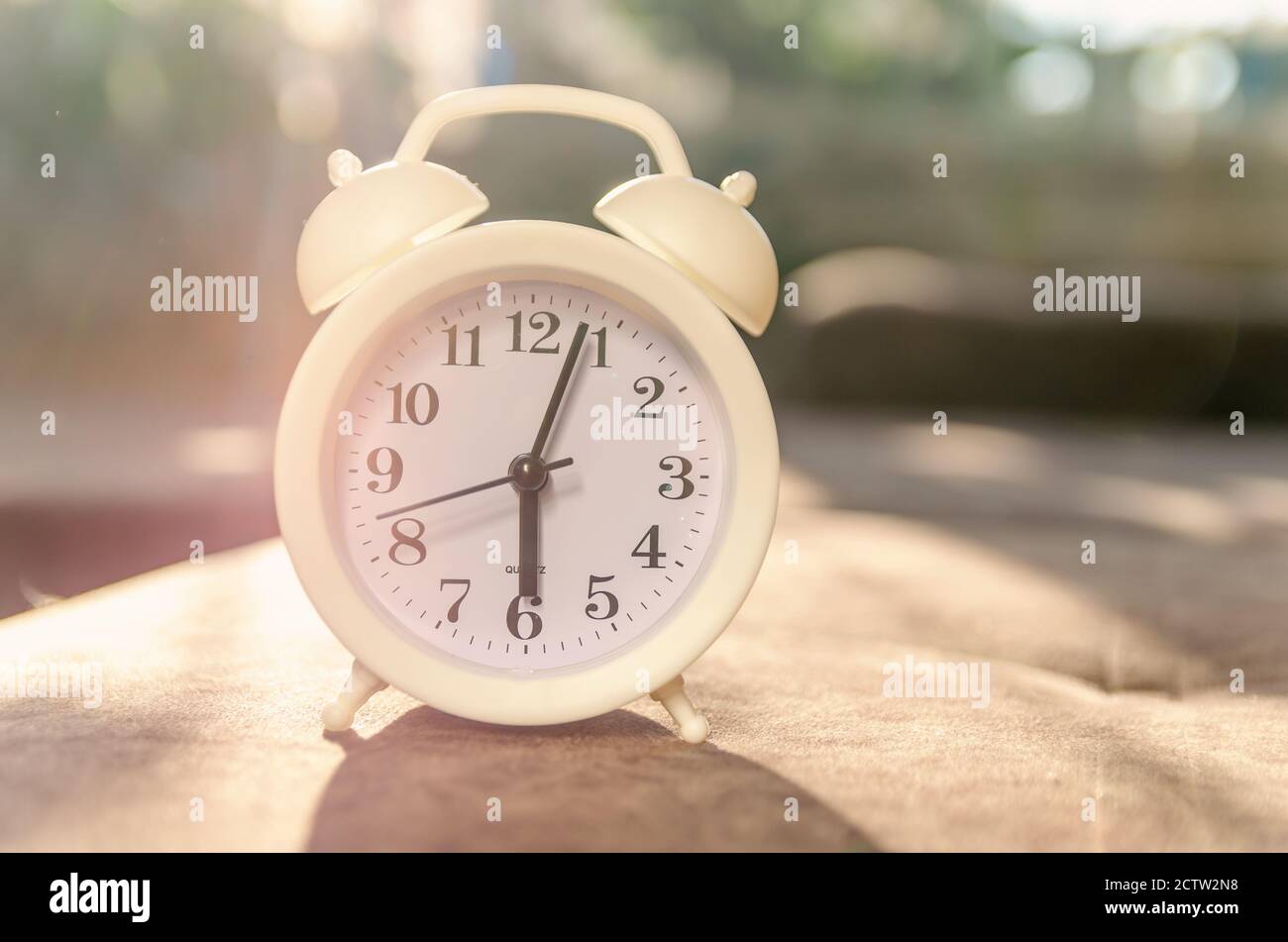 white alarm clock stands on the sofa in the sunlight. Beautiful ...