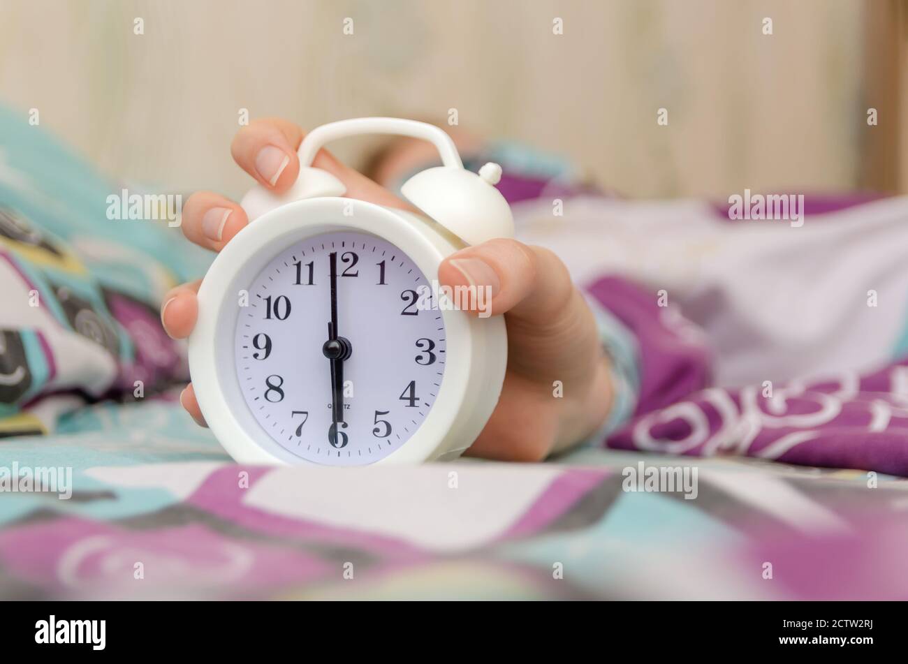 female hand holding white alarm clock lying in bed, early rise Stock ...