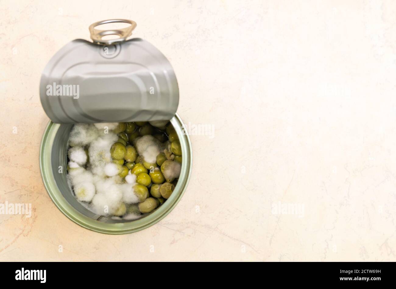 Open tin with green peas covered with mold on the table, top view ...