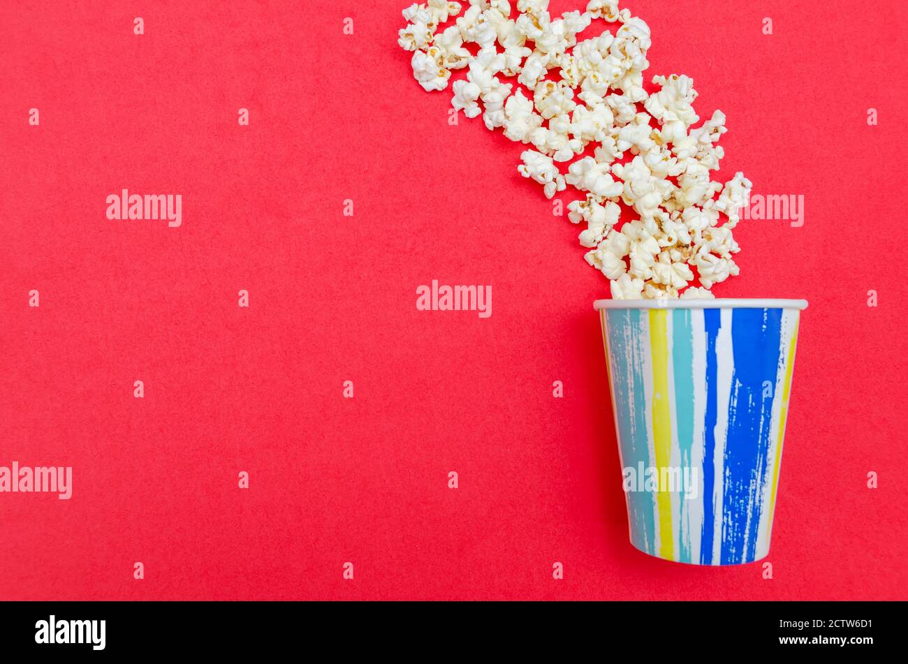 Spilled popcorn from a paper Cup on a red background, top view, copy ...