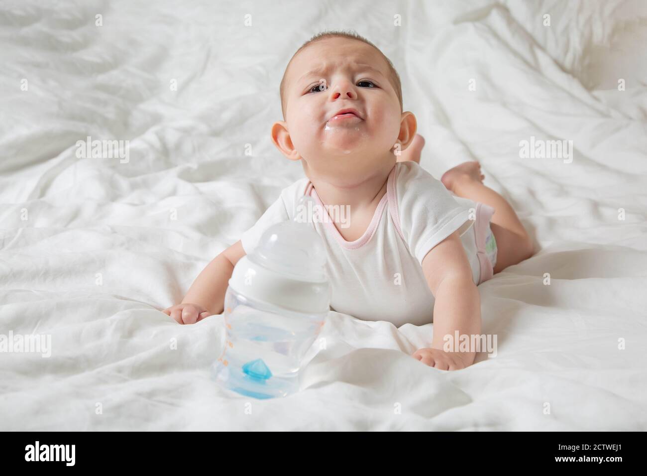 The baby is drooling and teething. He lies on a white bed and pulls his ...