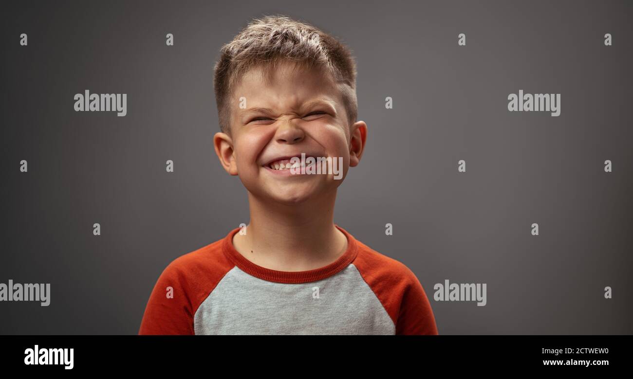 Funny boy squints and smiles at the camera. Boy winces his nose in the ...