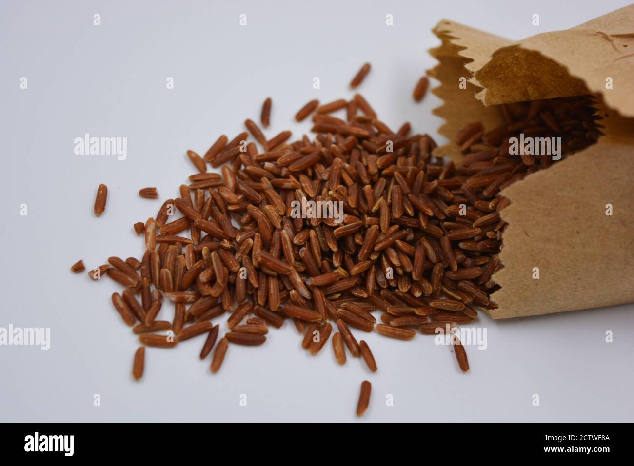Large healthy red long rice poured out of a brown paper bag on a white ...