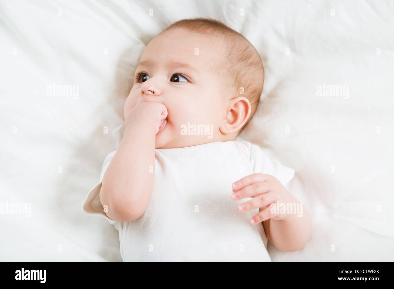 The baby teething Close up portrait of little baby girl in white lying ...