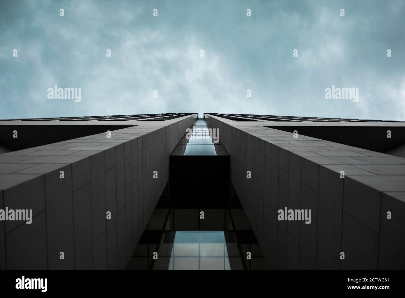 Looking up at symmetrical tall building with reflection of cloudy sky ...