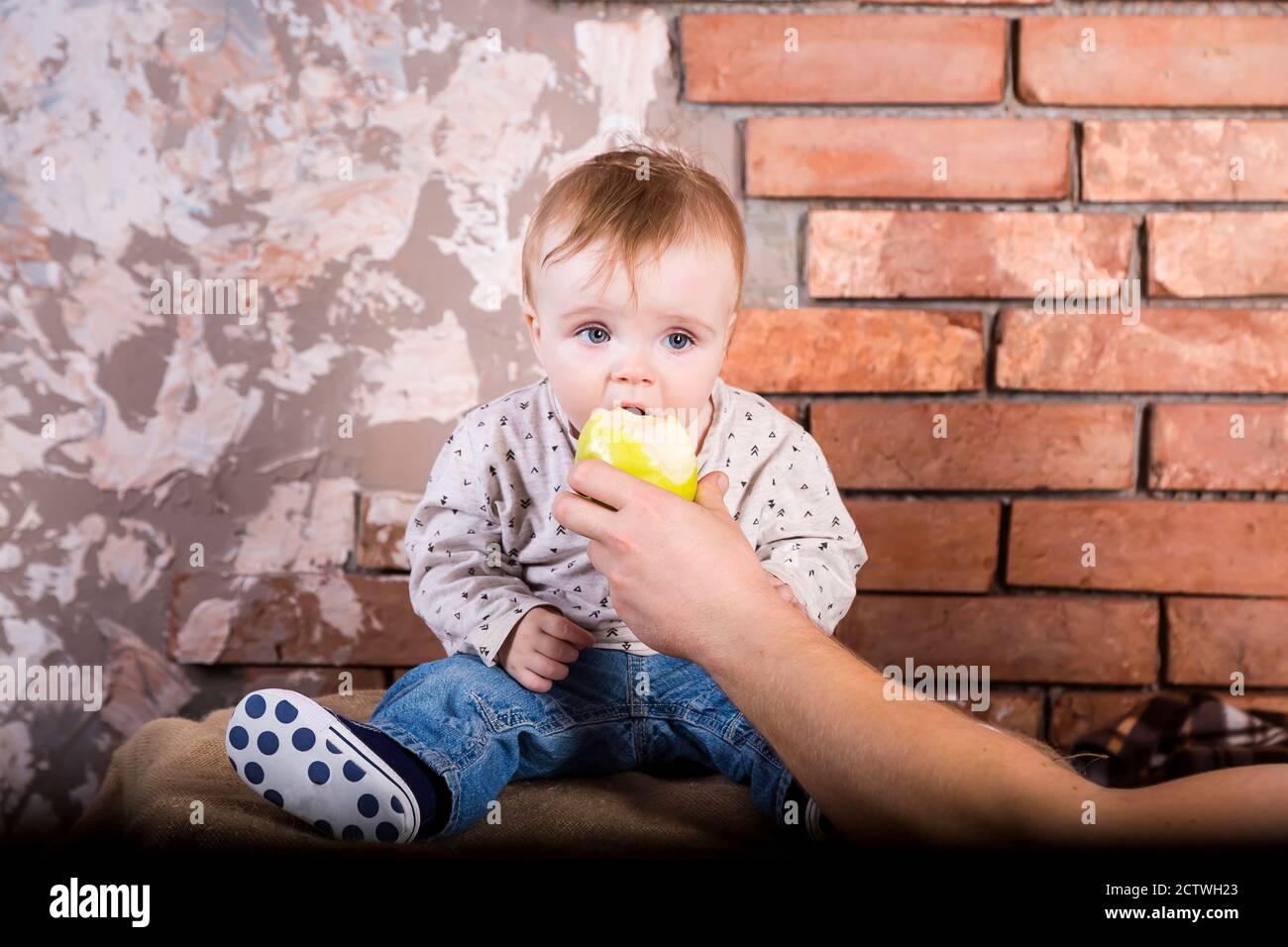 One year old child sits on a barrel against the background of a red ...