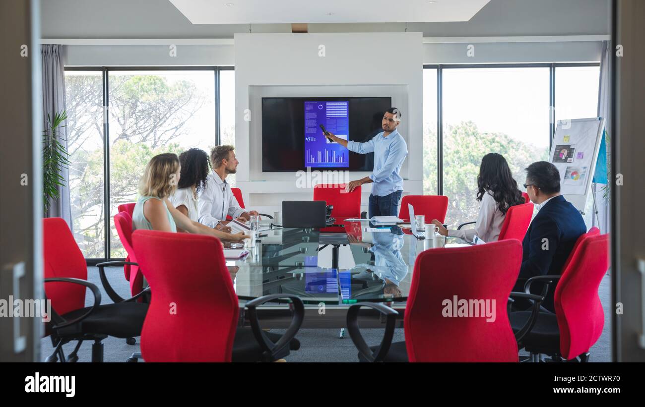 Mixed race businessman standing beside a screen giving a presentation ...