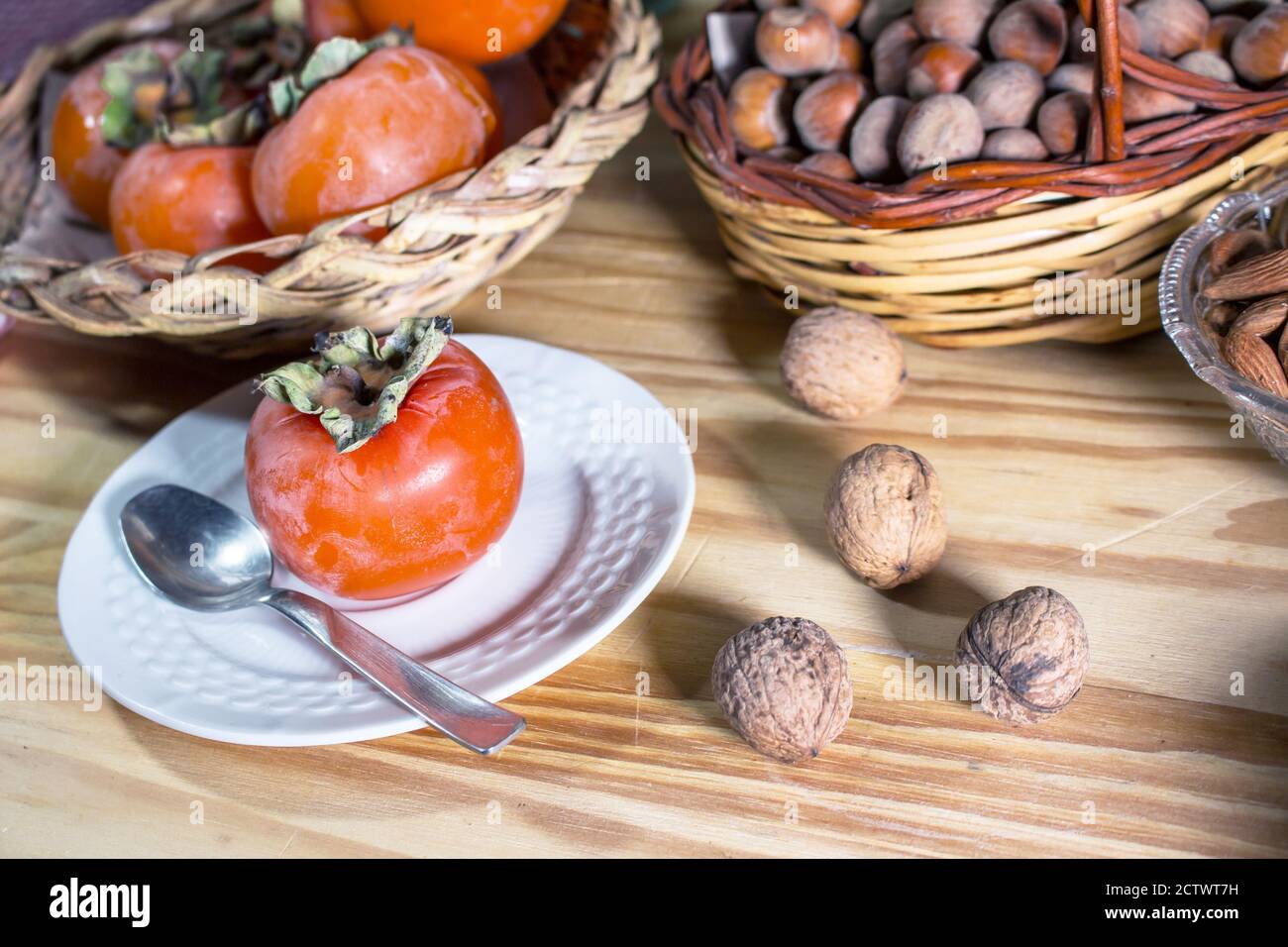 A persimmon served on a saucer with spoonfuls. In the background wicker ...