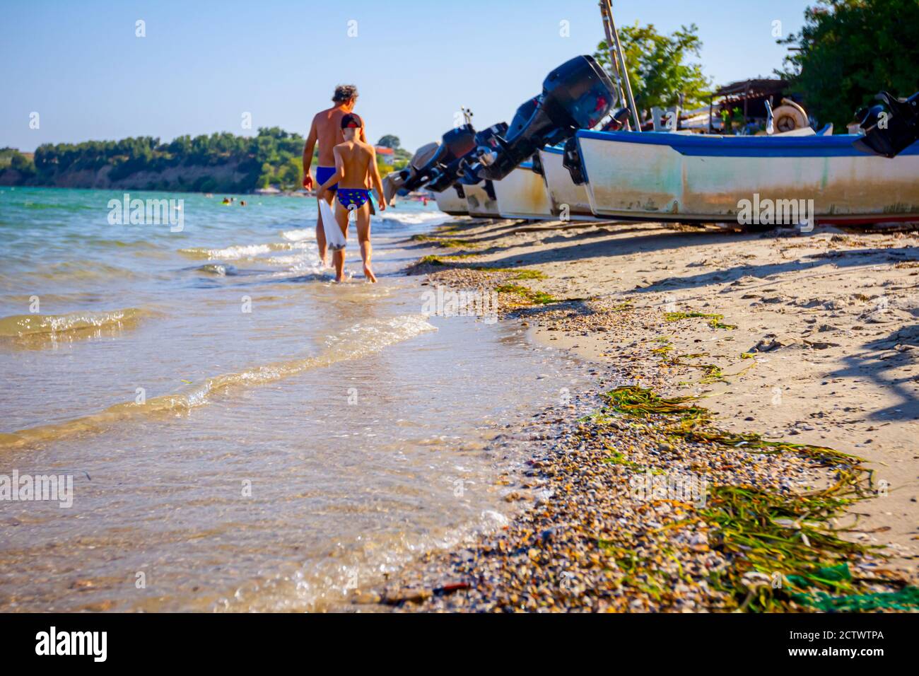 Fishing boats are dry docked on the sandy, pebbles beach, tourists pass ...
