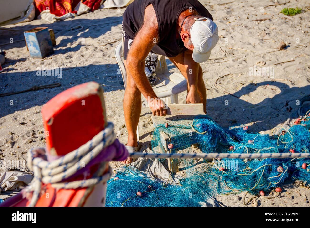 A fisherman is standing at the beach and cleaning fishing net from ...