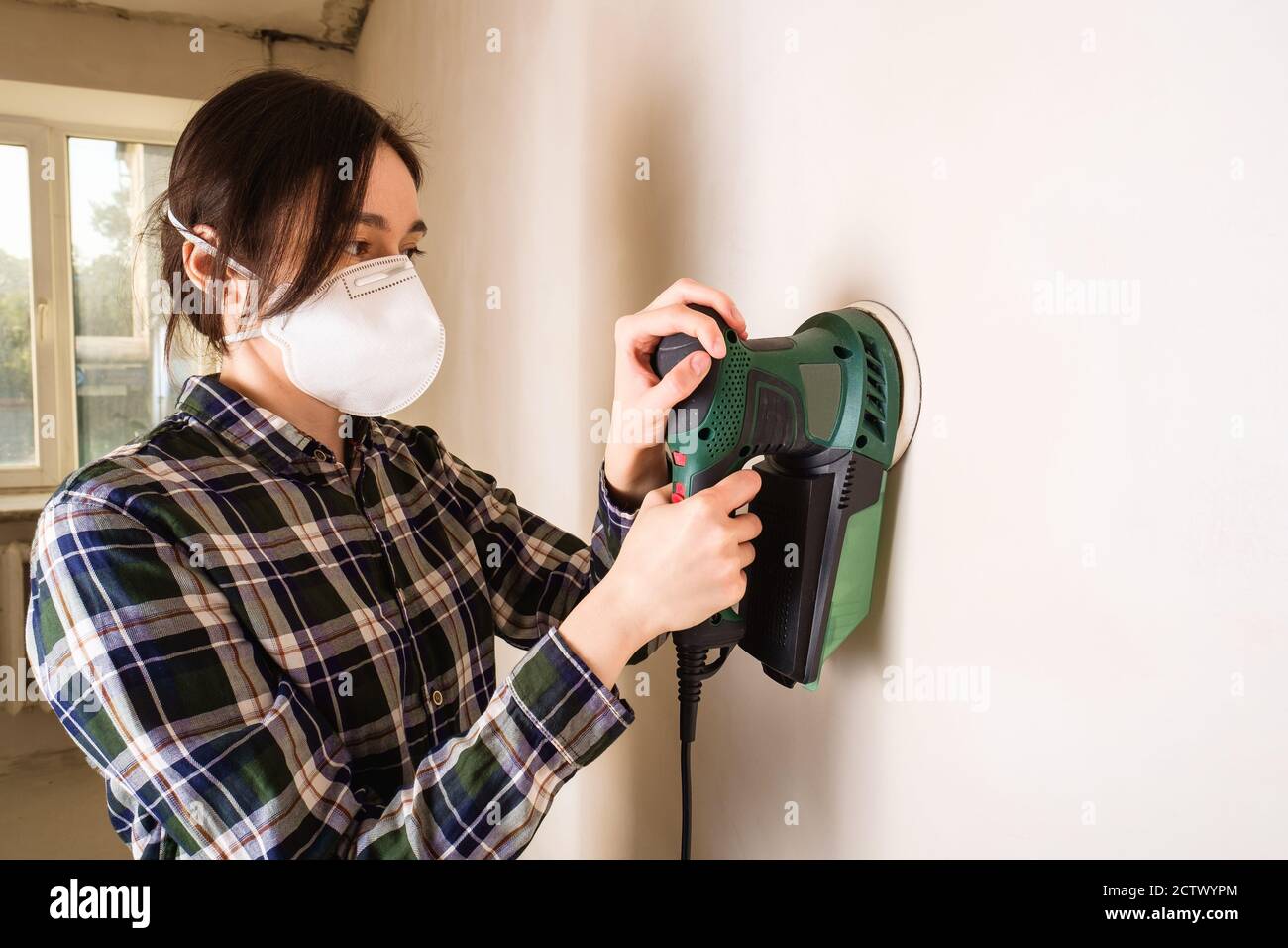 Woman in protective mask working with electric sander to smooth plaster ...