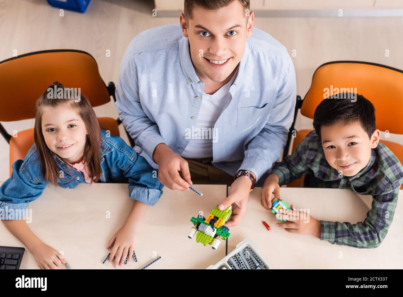 Overhead view of teacher and multiethnic pupils looking at camera while ...