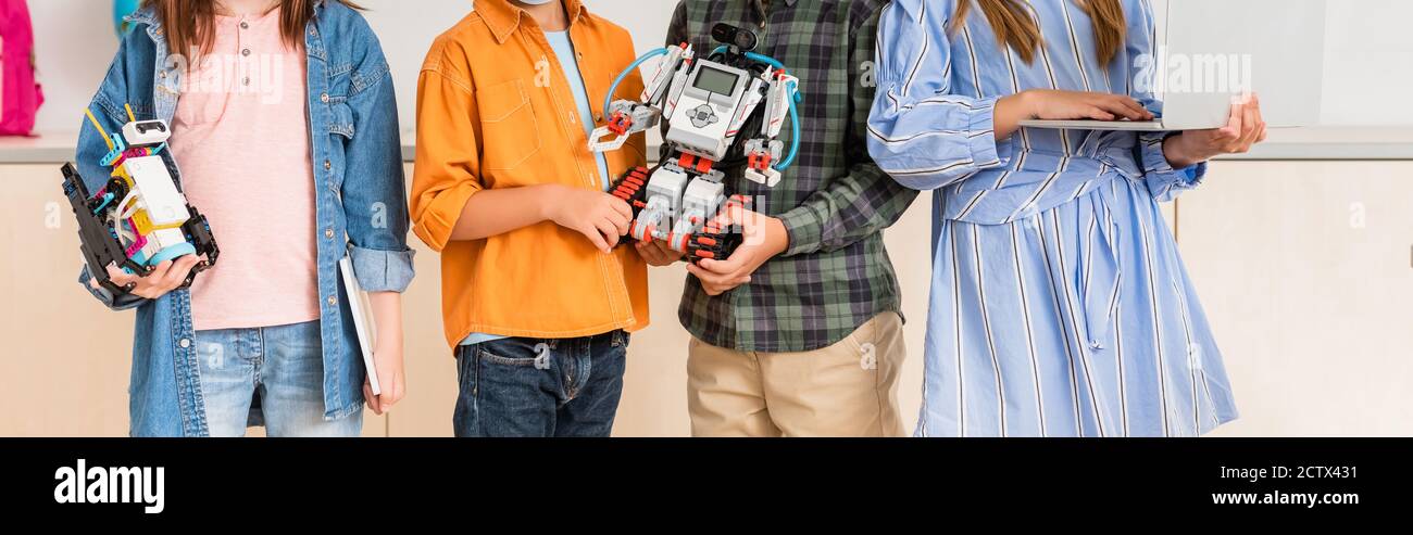 Panoramic shot of schoolkids holding robots and laptop in stem school ...