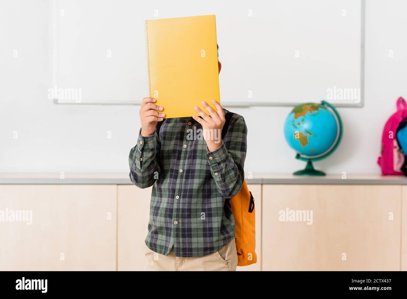 Schoolboy covering face with book in classroom of stem school Stock ...