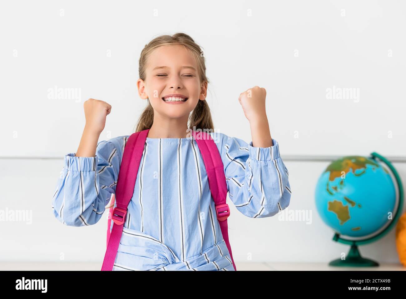Schoolgirl with backpack showing yeah gesture in classroom Stock Photo ...