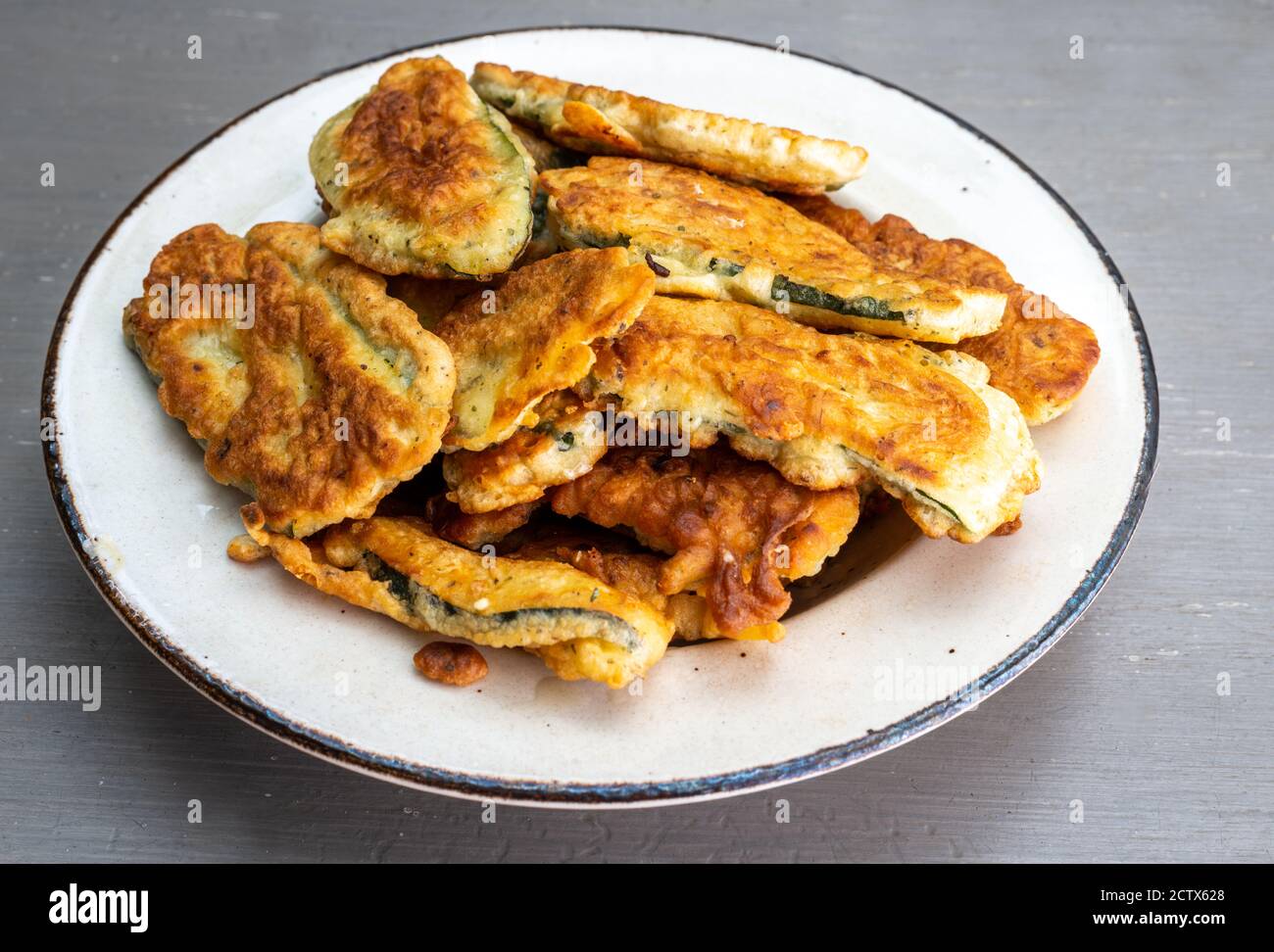 A pile of Courgette fritters in batter in a plate on grey table Stock ...