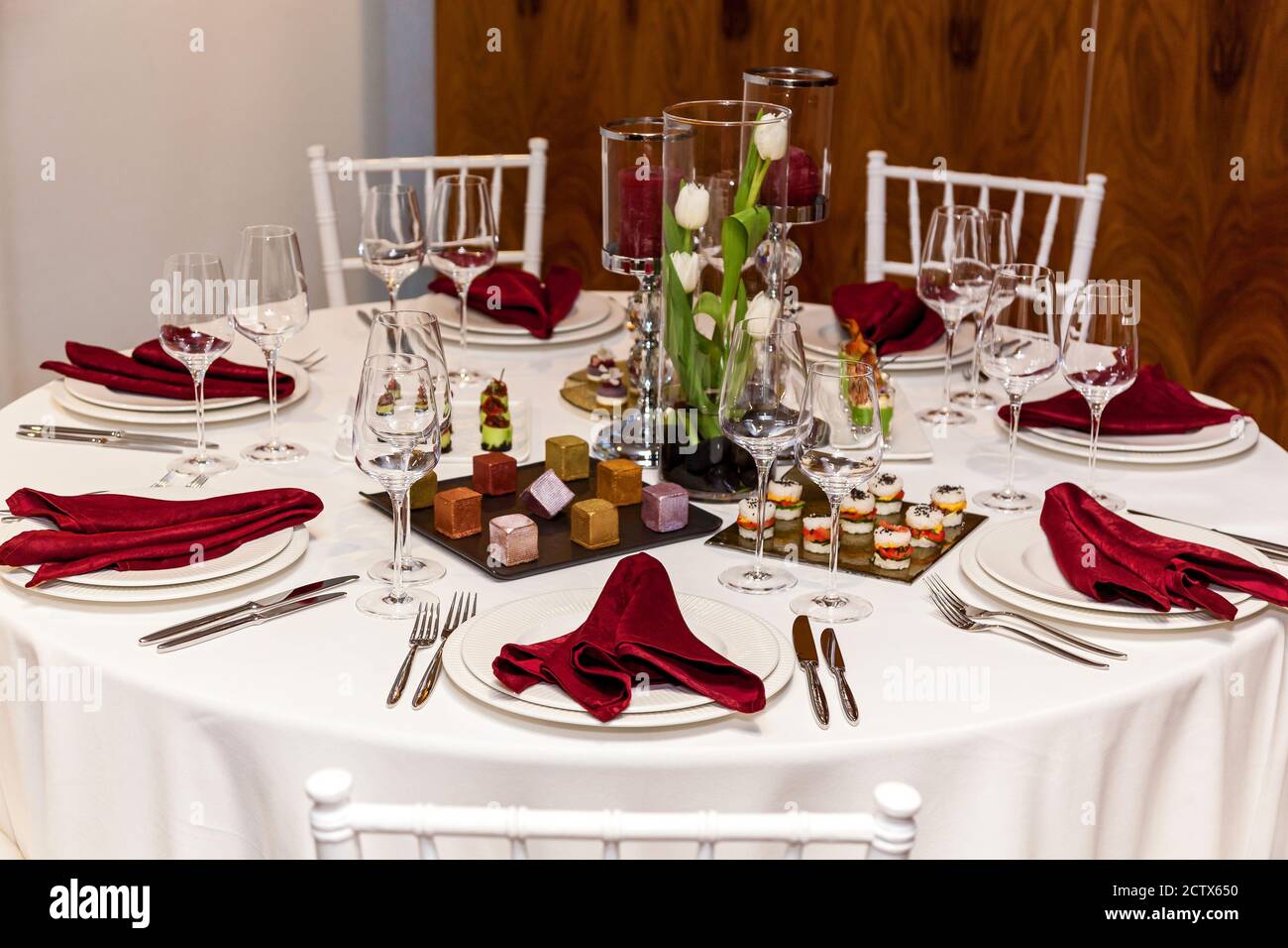 Round table with white tablecloth and red napkins, set of cutlery with ...