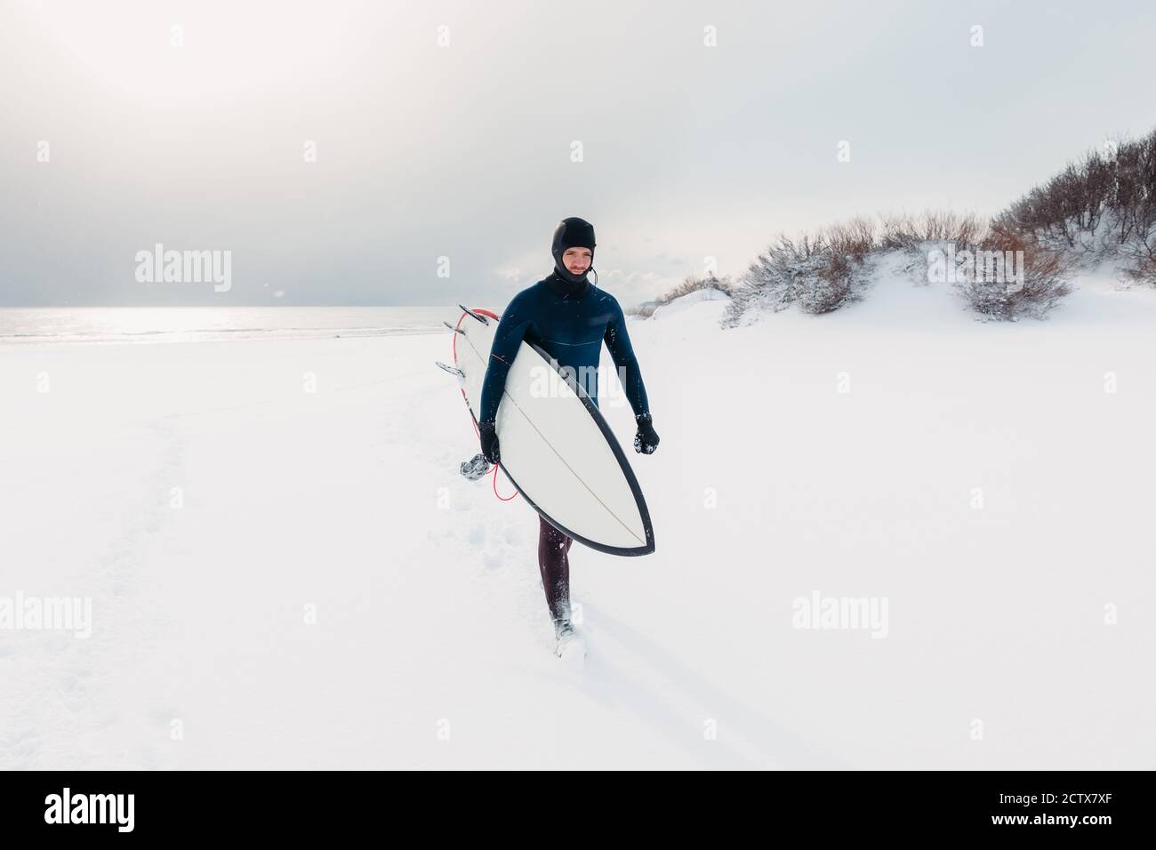 Winter and surfer with surfboard. Snowy beach with male surfer in ...