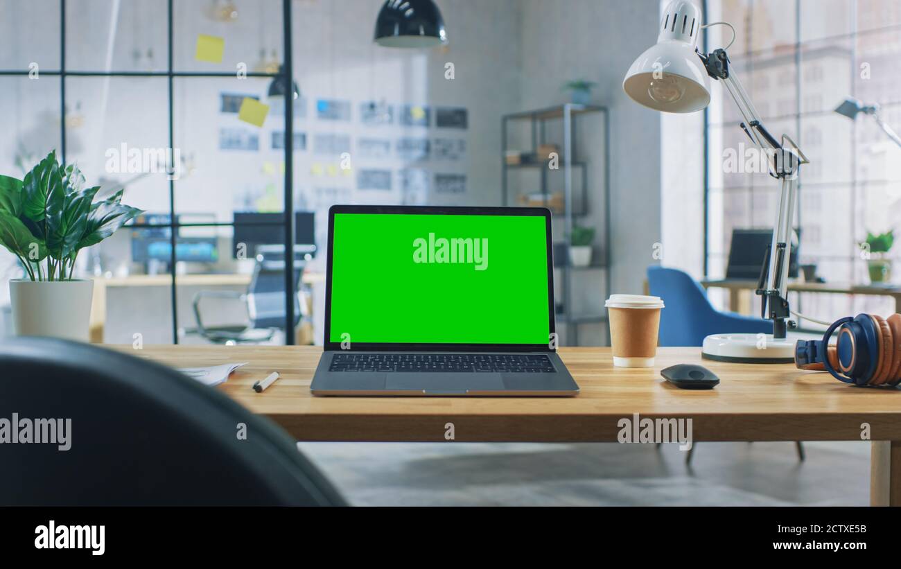 Laptop on the Desk in the Office Shows Green Mock-up Screen. In the ...