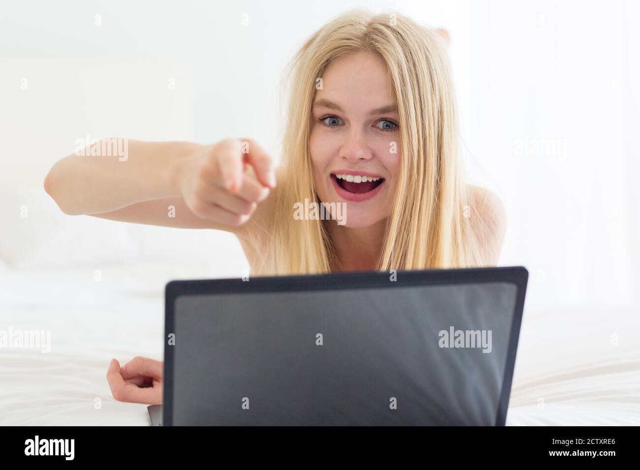 Happy young woman pointing her finger towards the camera while using a ...