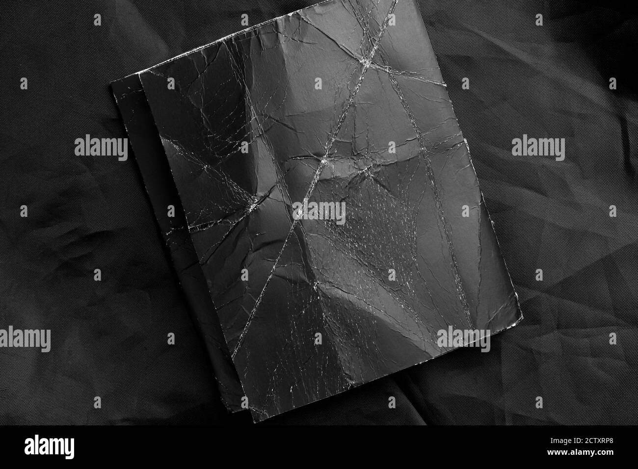 Folded black wrinkled cardboard on dark wrinkled synthetic material ...