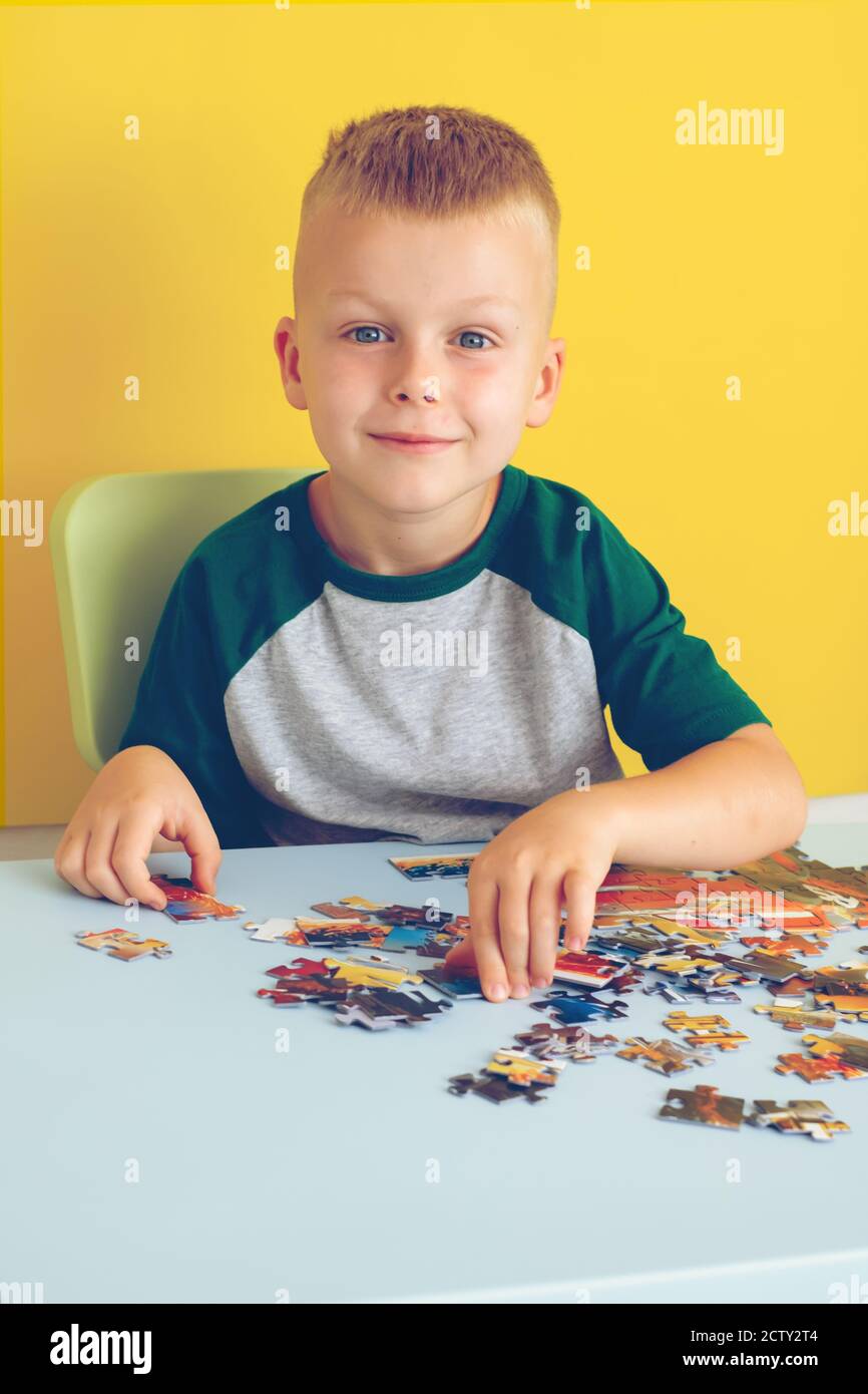 Portrait of a cute boy sitting at the table and putting together ...