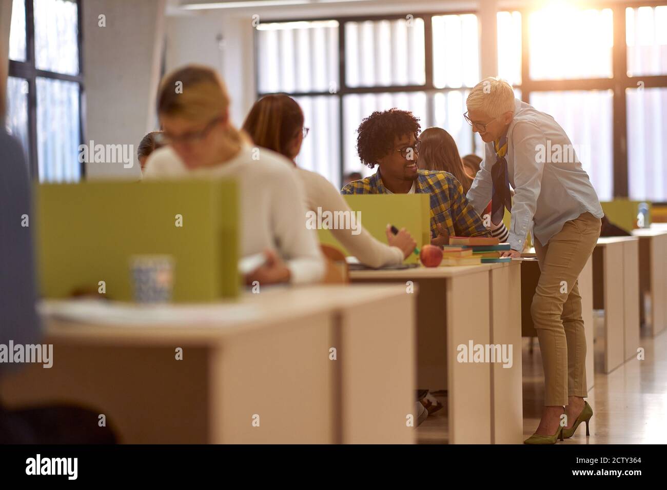 Female professor checking student work at a lecture in a classroom ...