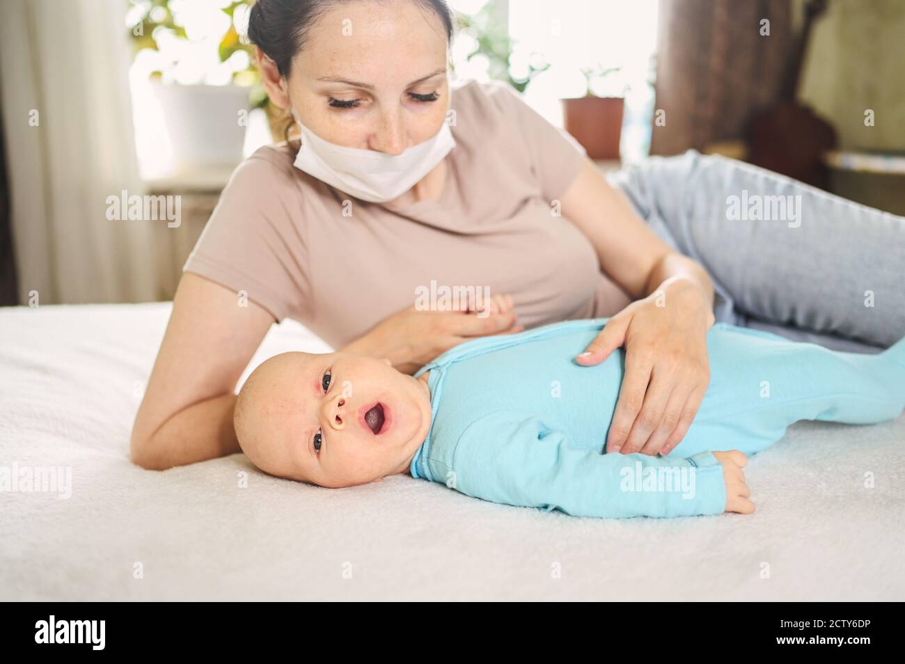 Beautiful mother in protective face mask holding her little cute ...