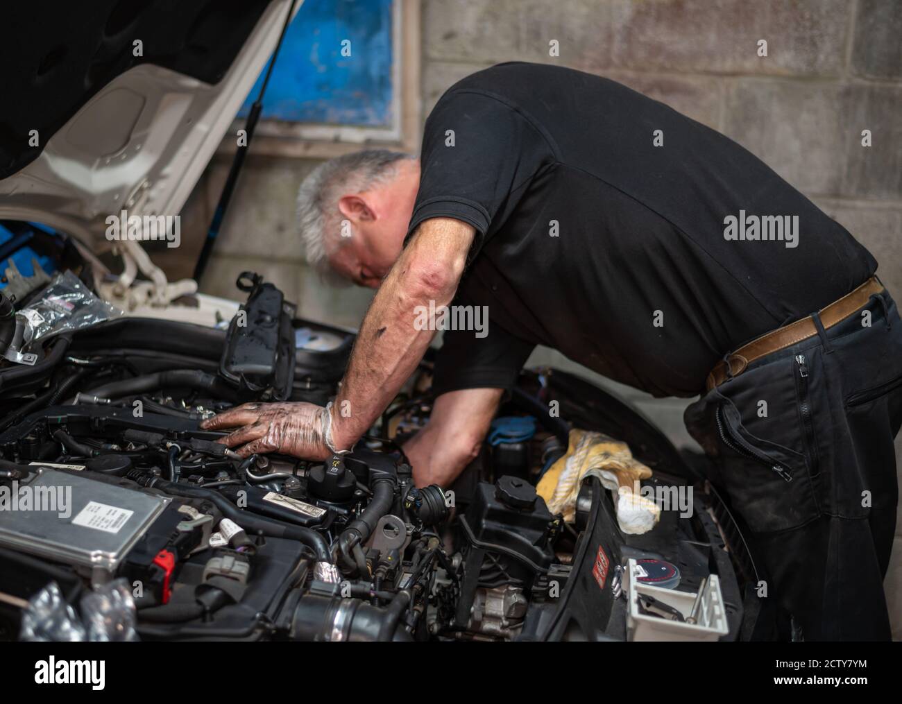 Senior Mechanic working on engine bay repairing a oil leak in home ...