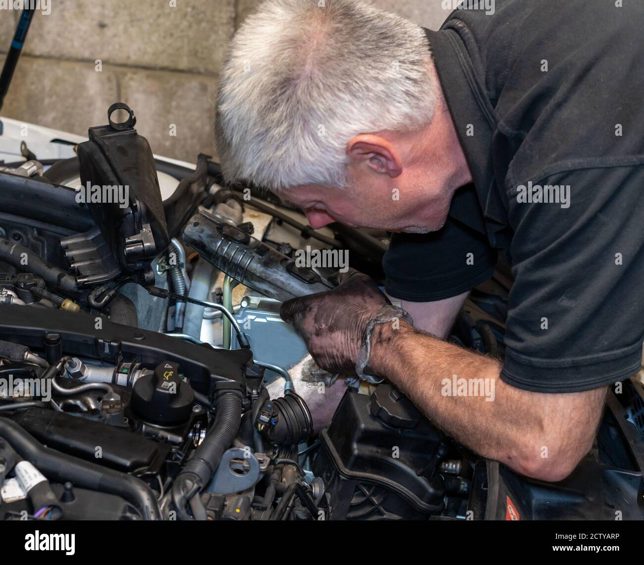 Senior Mechanic working on engine bay repairing a oil leak in home ...