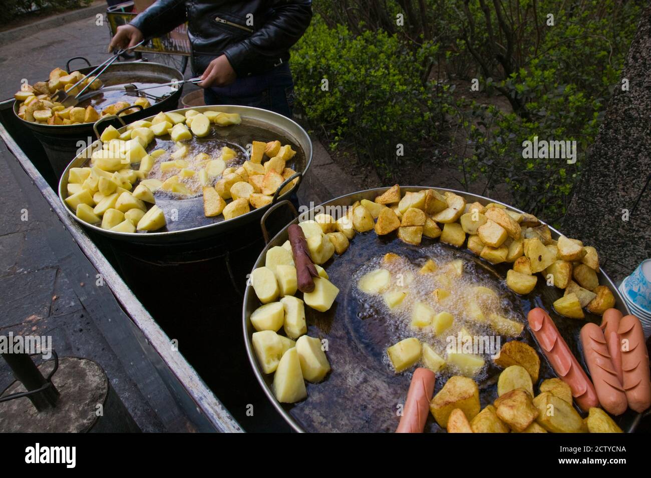 Vendor selling deep fried potatoes and sausages at a sidewalk food ...