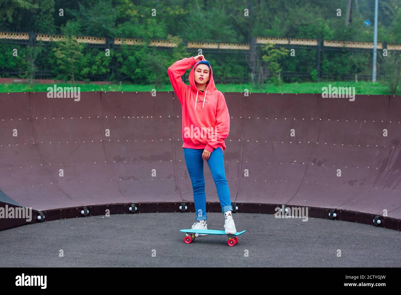 Portrait of a trendy pretty young girl standing next to the skateboard ...