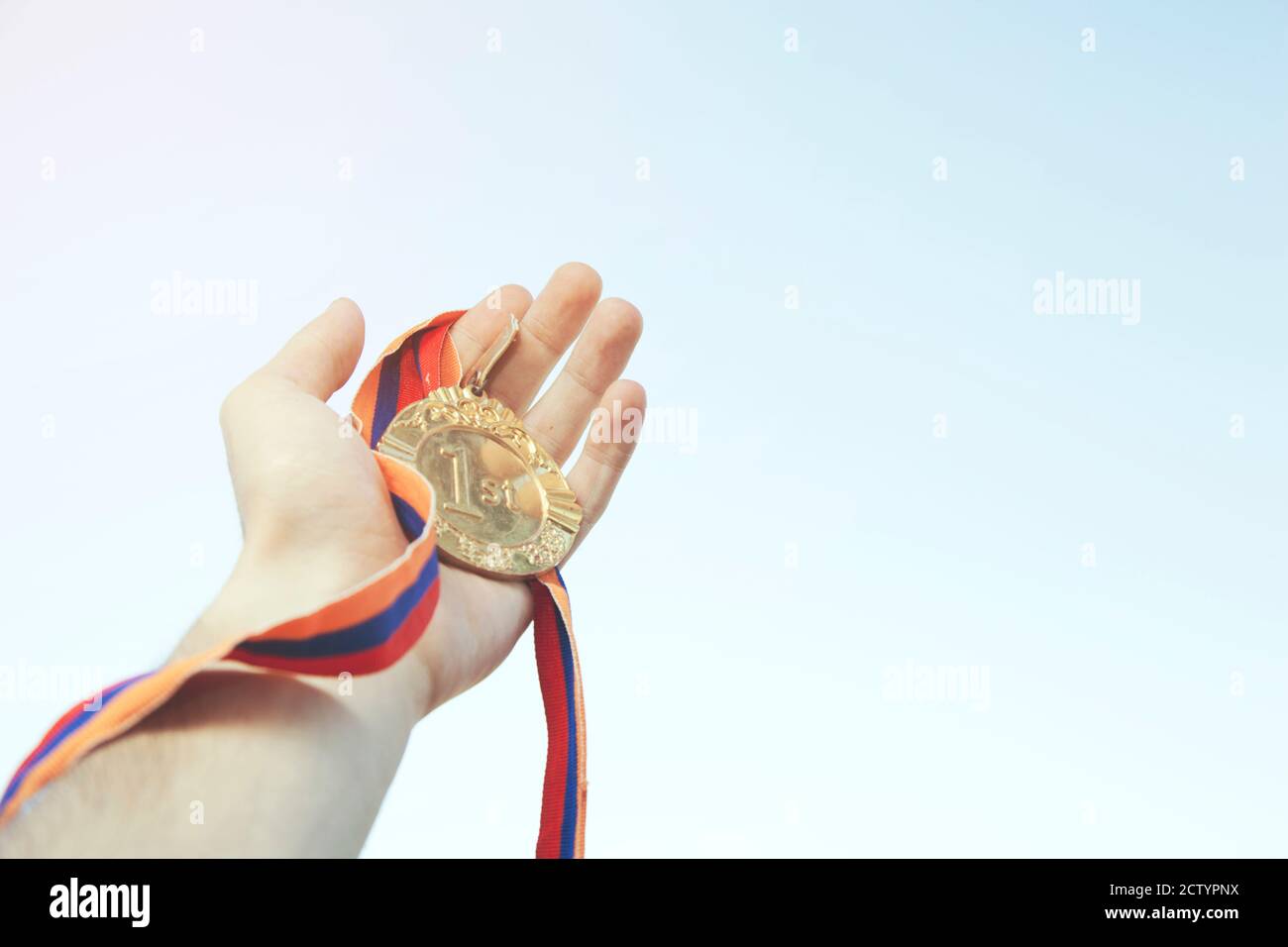 man hand raised, holding gold medal against sky Stock Photo - Alamy