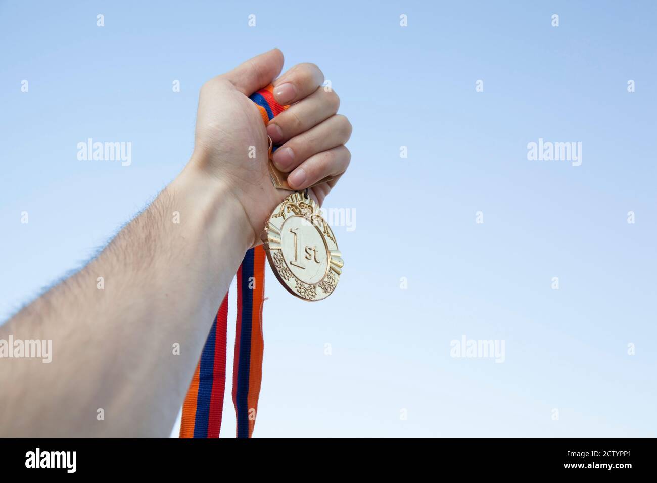 man hand raised, holding gold medal against sky Stock Photo - Alamy
