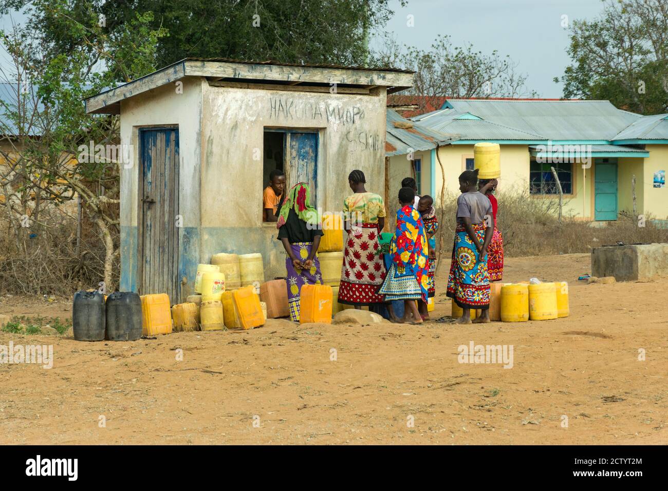 A group of African women and children queue to fill up water containers ...