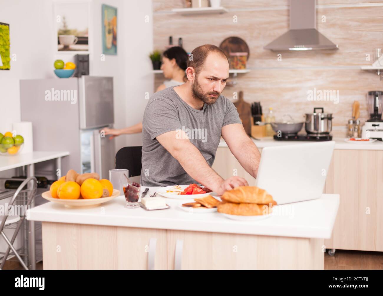 Furious freelancer working from home sitting on kitchen table while his ...