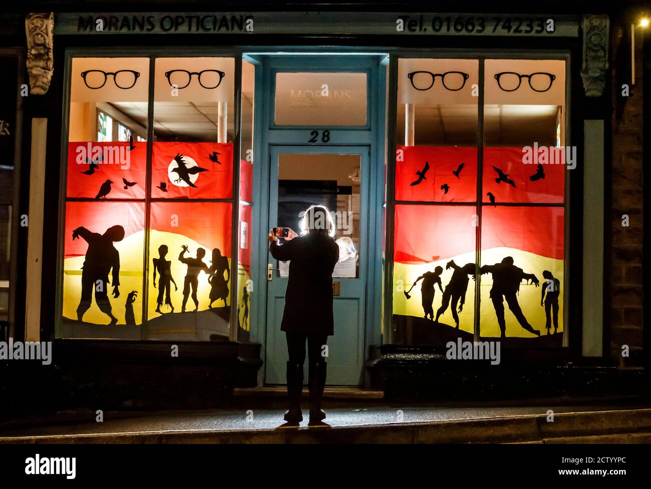 A woman takes a photograph of a decorated shop front during the Light ...