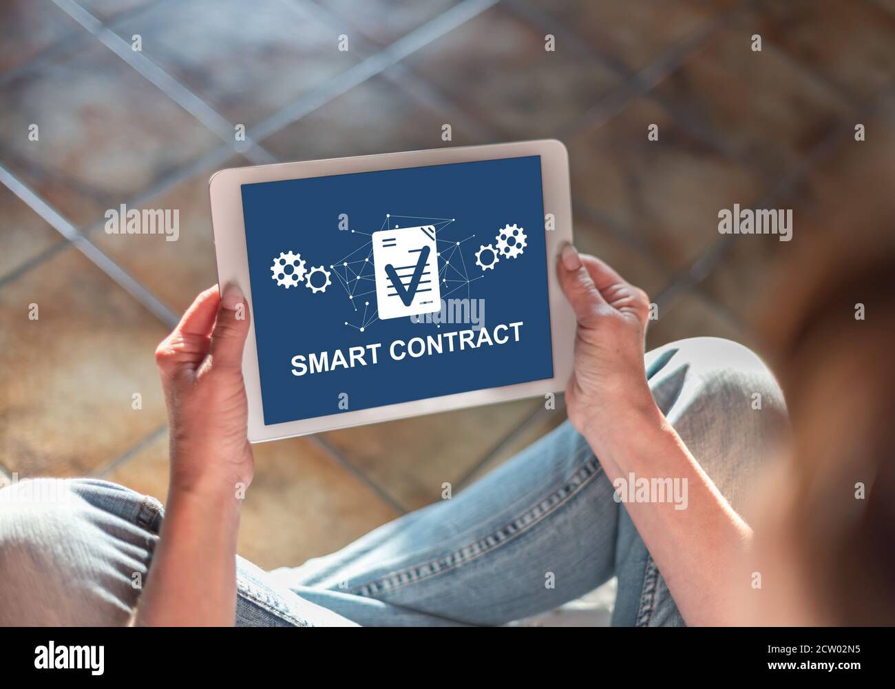 Woman sitting on the floor with a tablet showing smart contract concept ...
