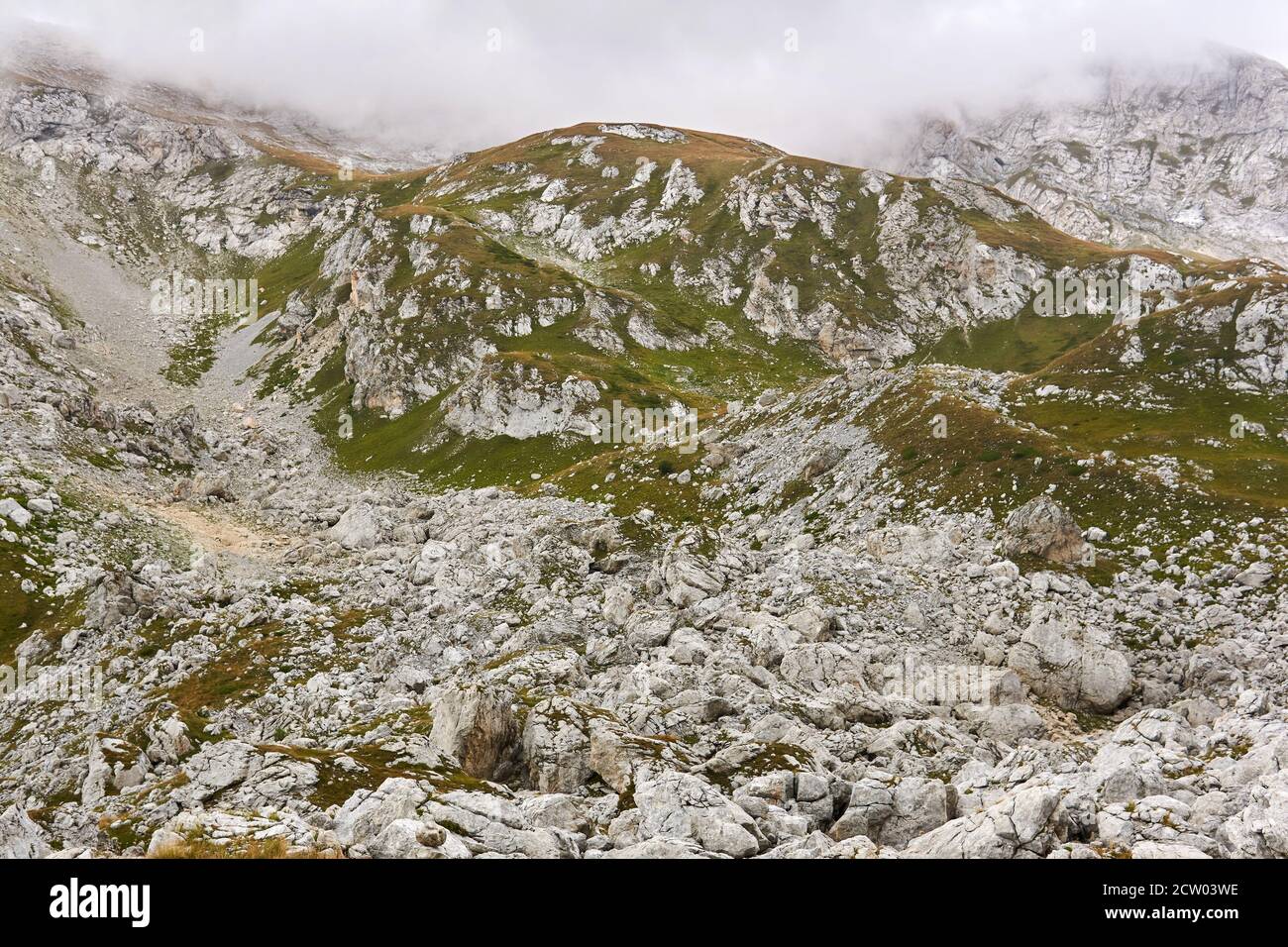 mountain landscape - rocky alpine slope partially hidden by a cloud ...