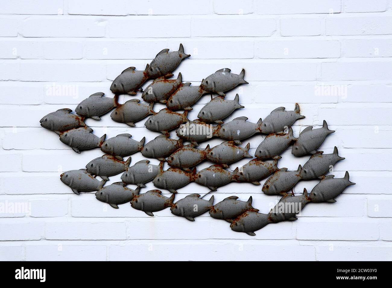 Metal fish decoration on a white brick wall Stock Photo - Alamy