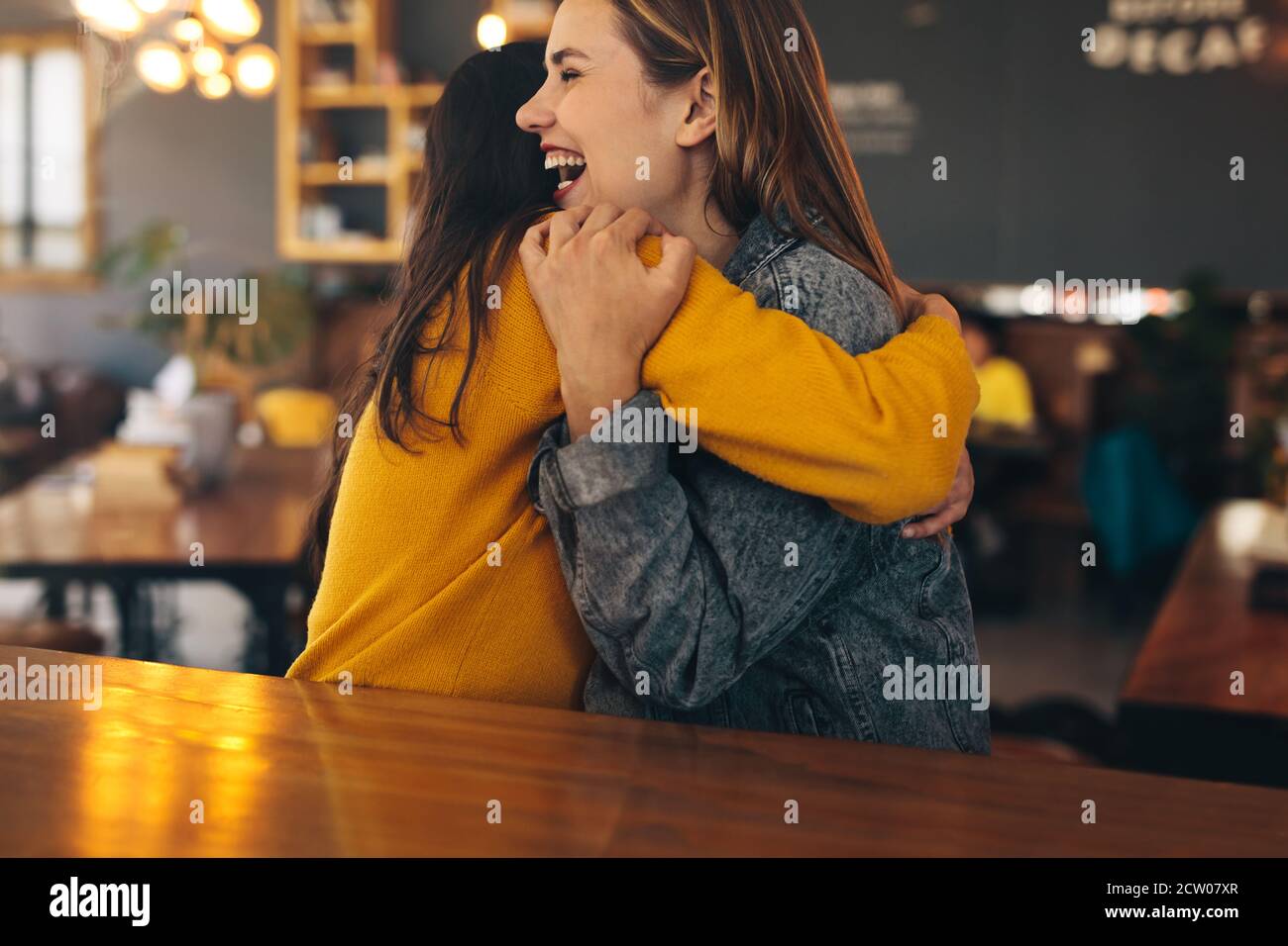 Two young women meeting at a coffee shop. Friends hugging each other at ...