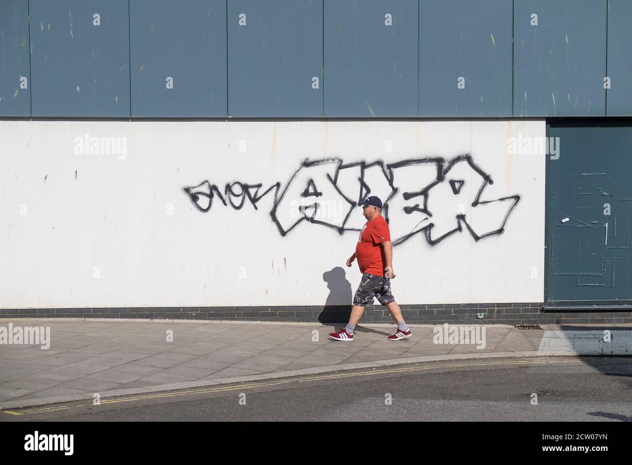 An overweight male holidaymaker walking past a wall sprayed with ugly ...