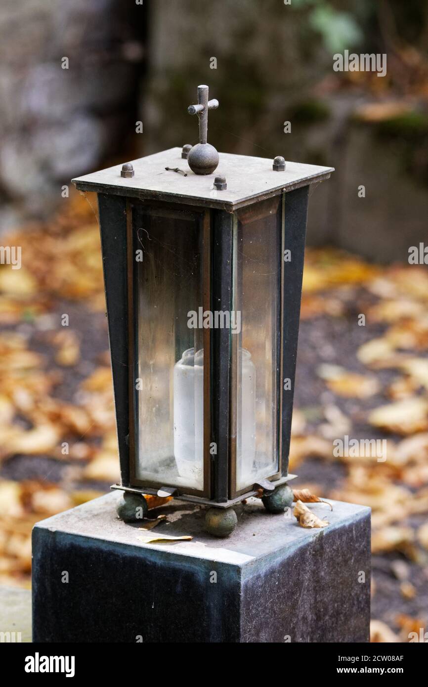 metal grave lantern with glass windows on a stone base in front of a blurred background with ...