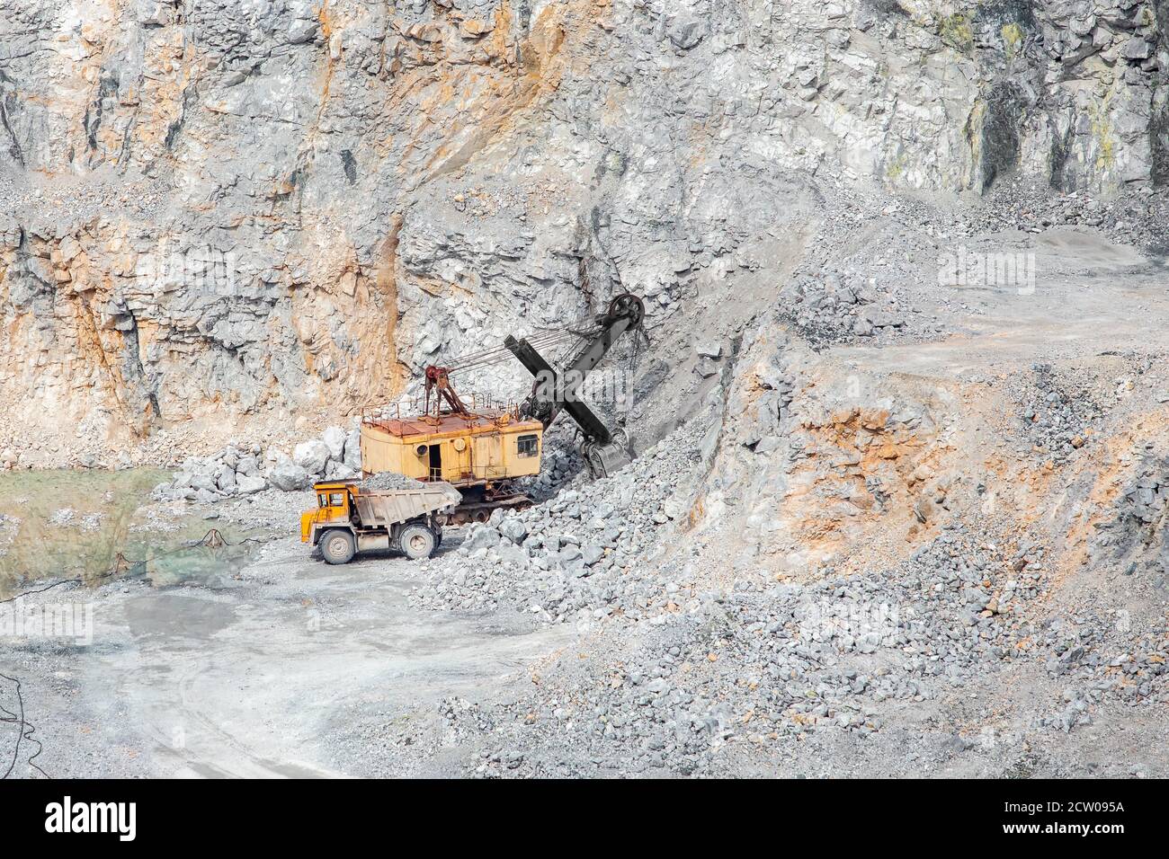 Excavator is loading raw materials into yellow truck for transport to ...