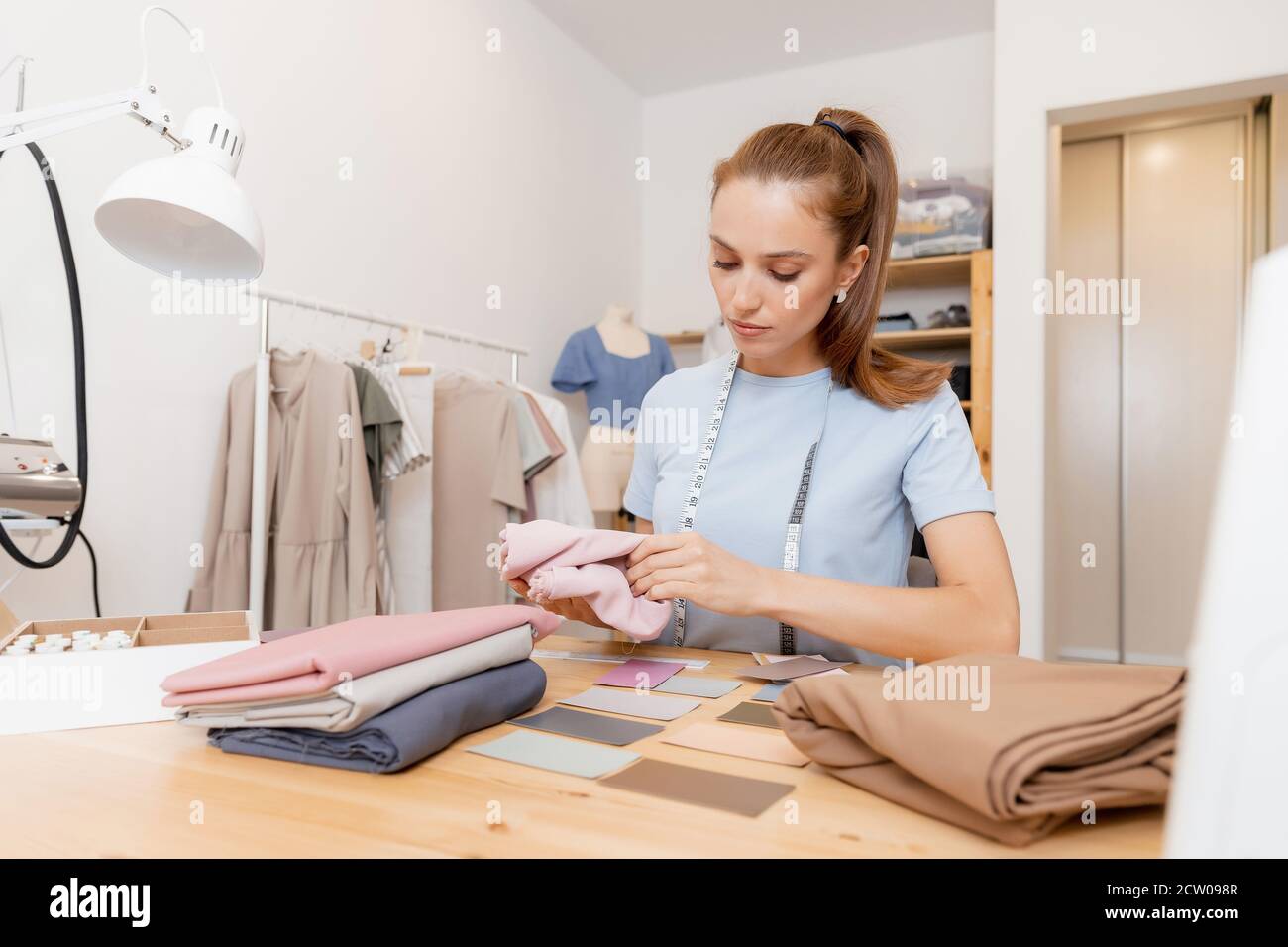 Young woman tailor fashion designer chooses shades of fabric and forms ...