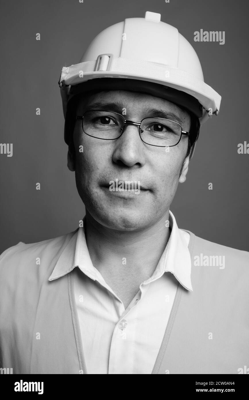 Young Asian man construction worker wearing eyeglasses against gray ...